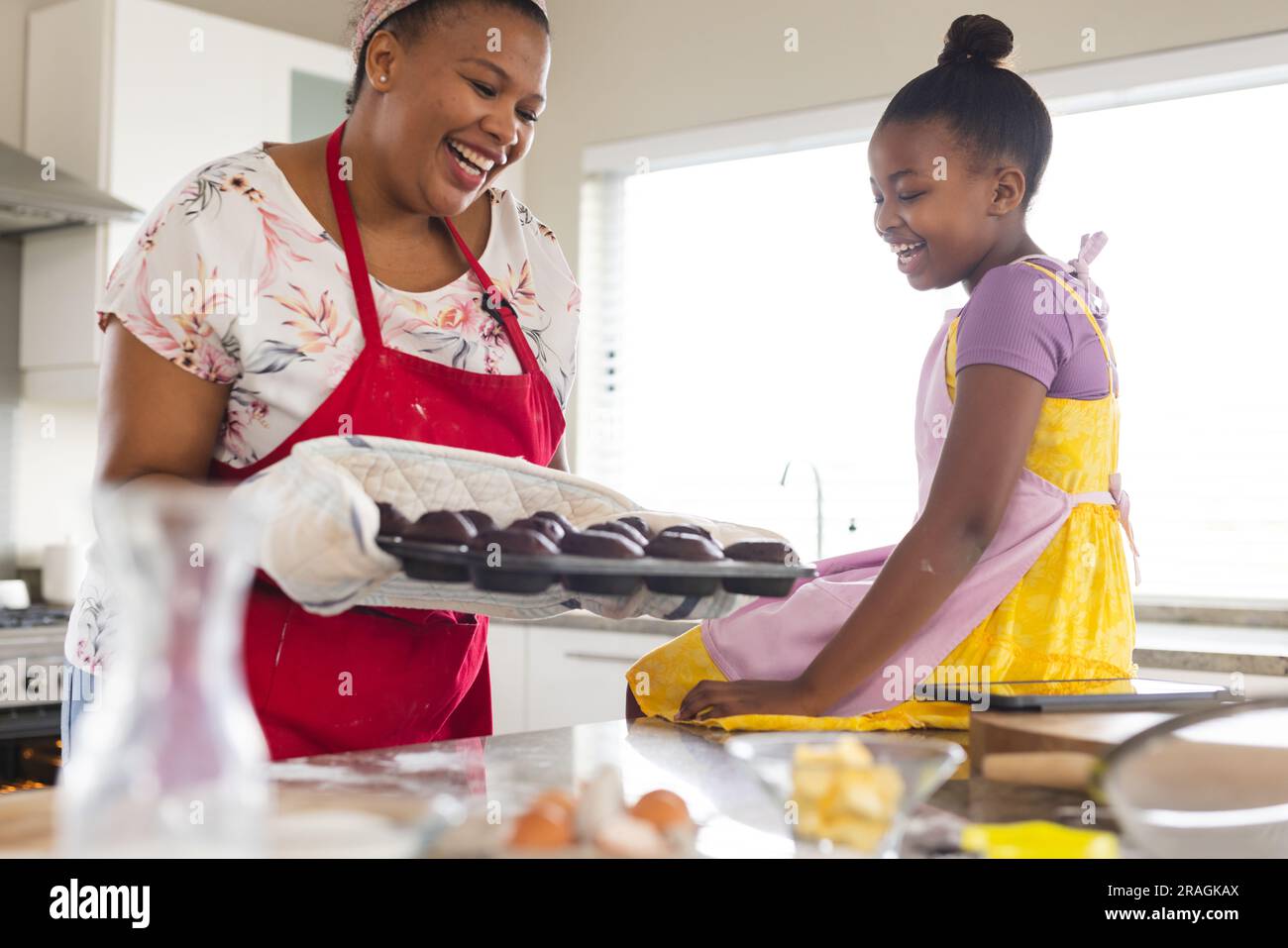 Happy african american mother and daughter baking cupcakes, taking ...