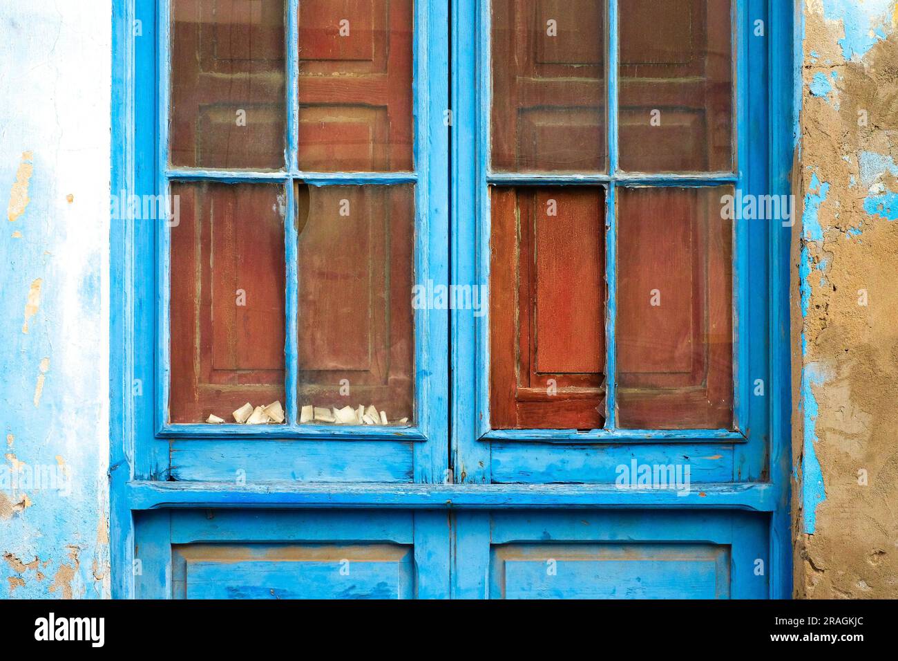 Blue weathered window frame with broken glass and aged wall sections ...