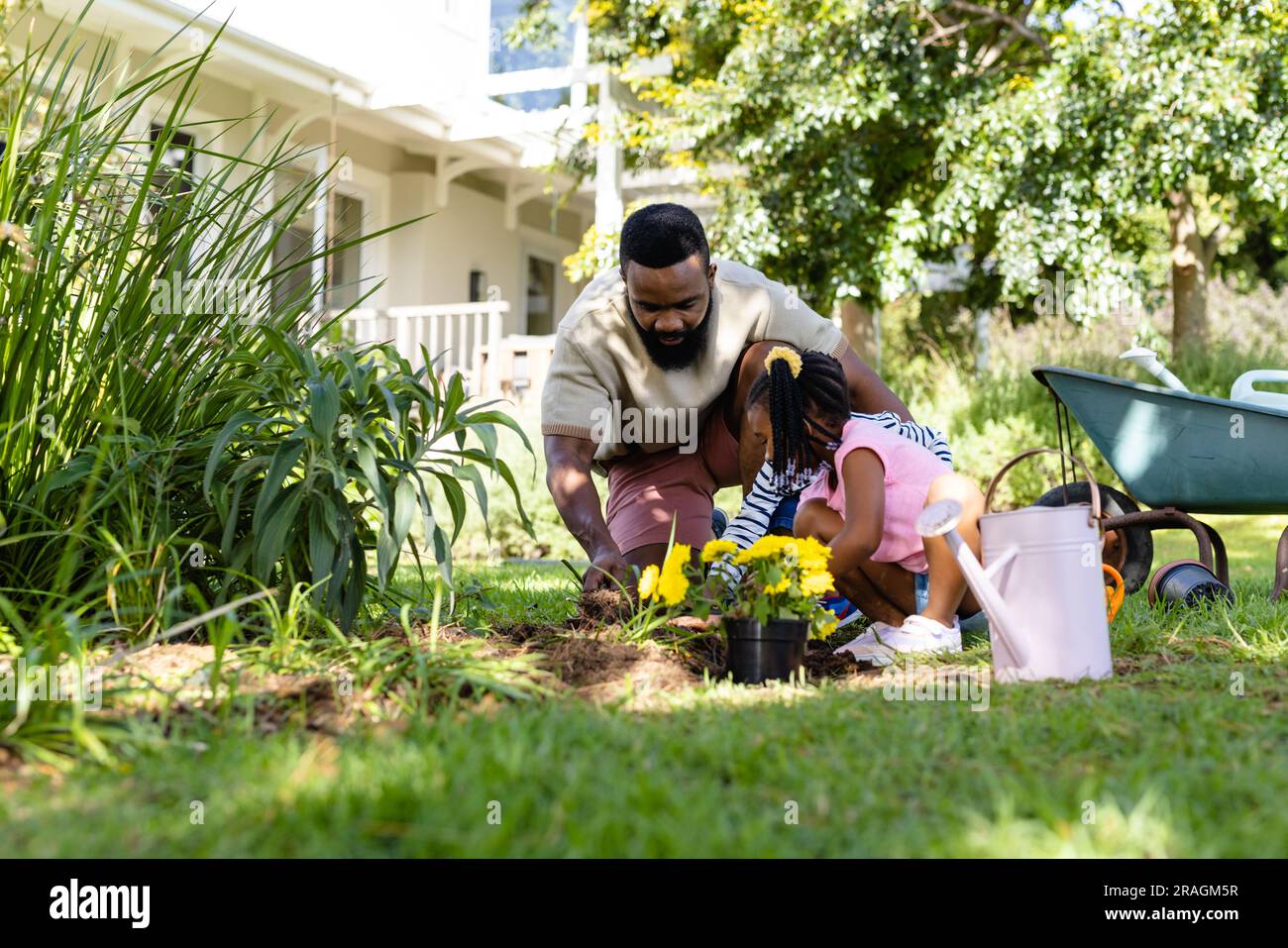 African american father planting flowers with daughter and son on field ...