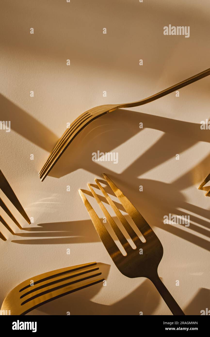 Golden forks on the white table in natural light with long shadows ...