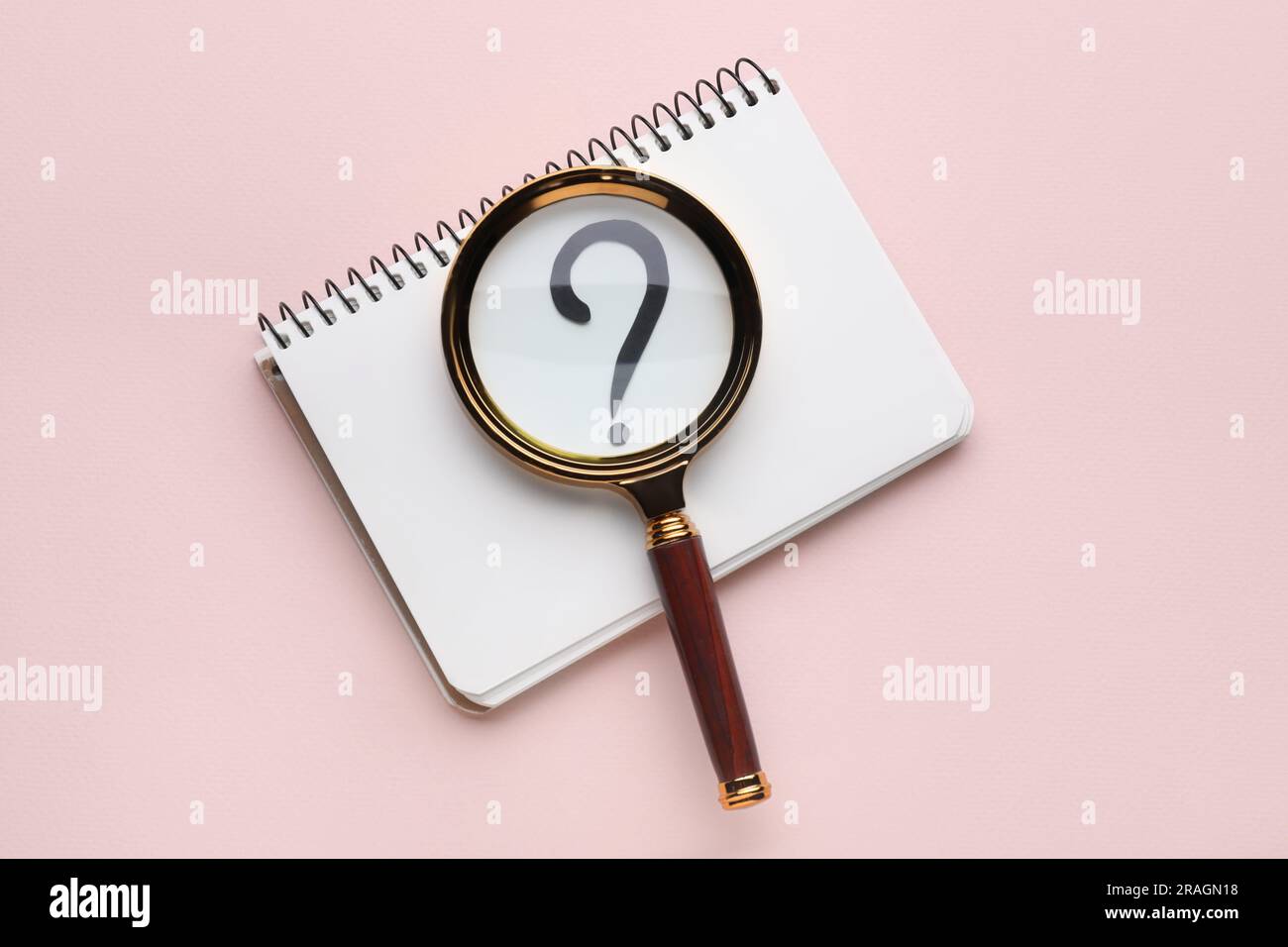 Magnifying glass over notebook with question mark on light pink ...