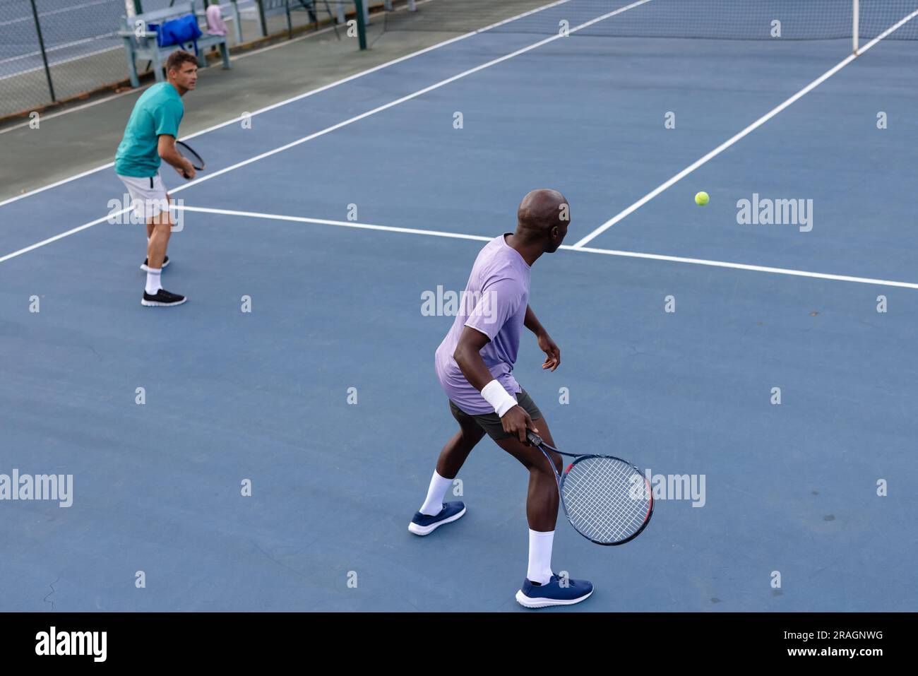 Diverse male tennis players playing doubles on outdoor court Stock ...
