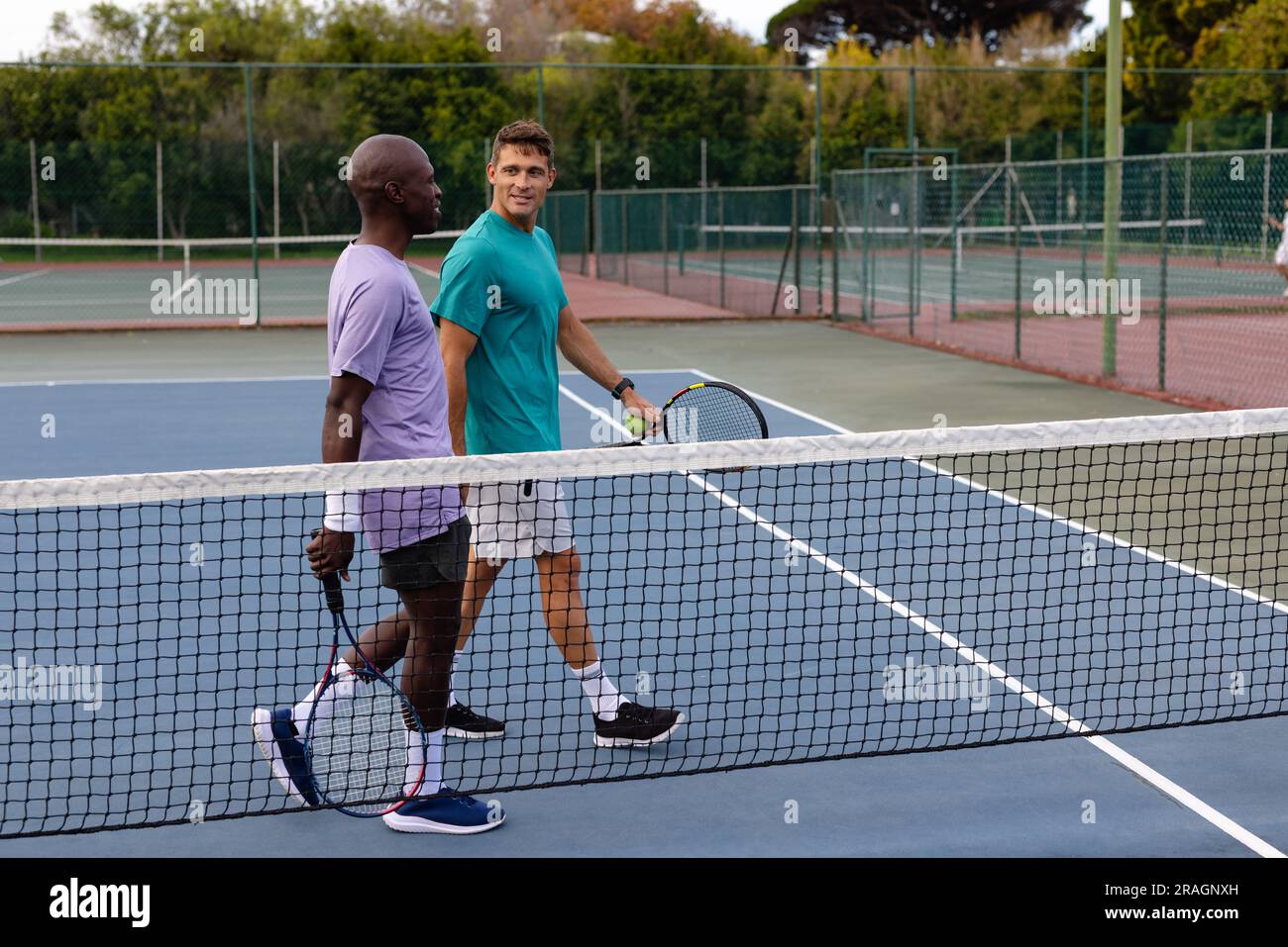 Happy diverse male tennis players walking with tennis rackets at ...
