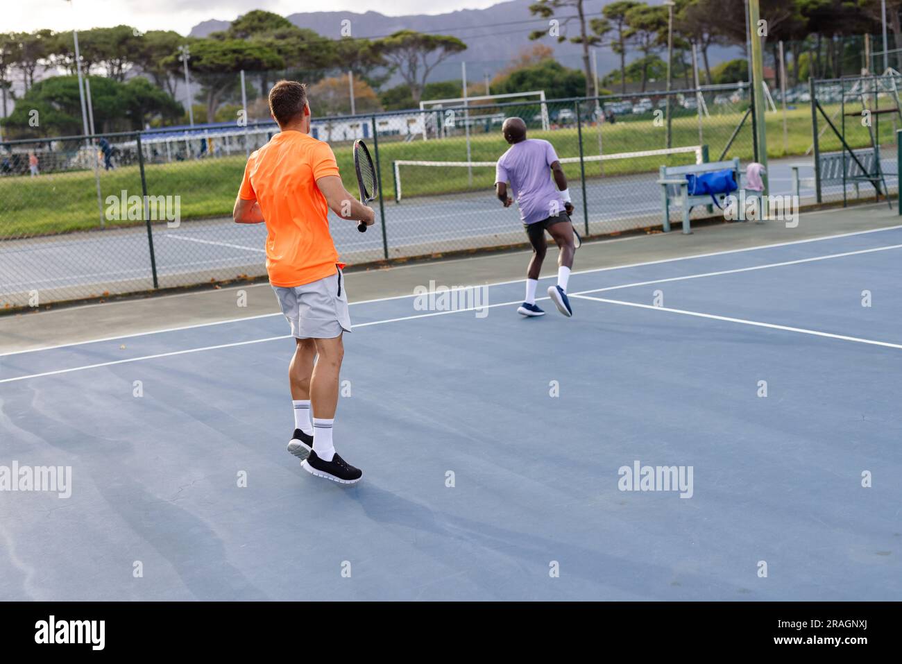Diverse male tennis players playing doubles on outdoor court Stock ...