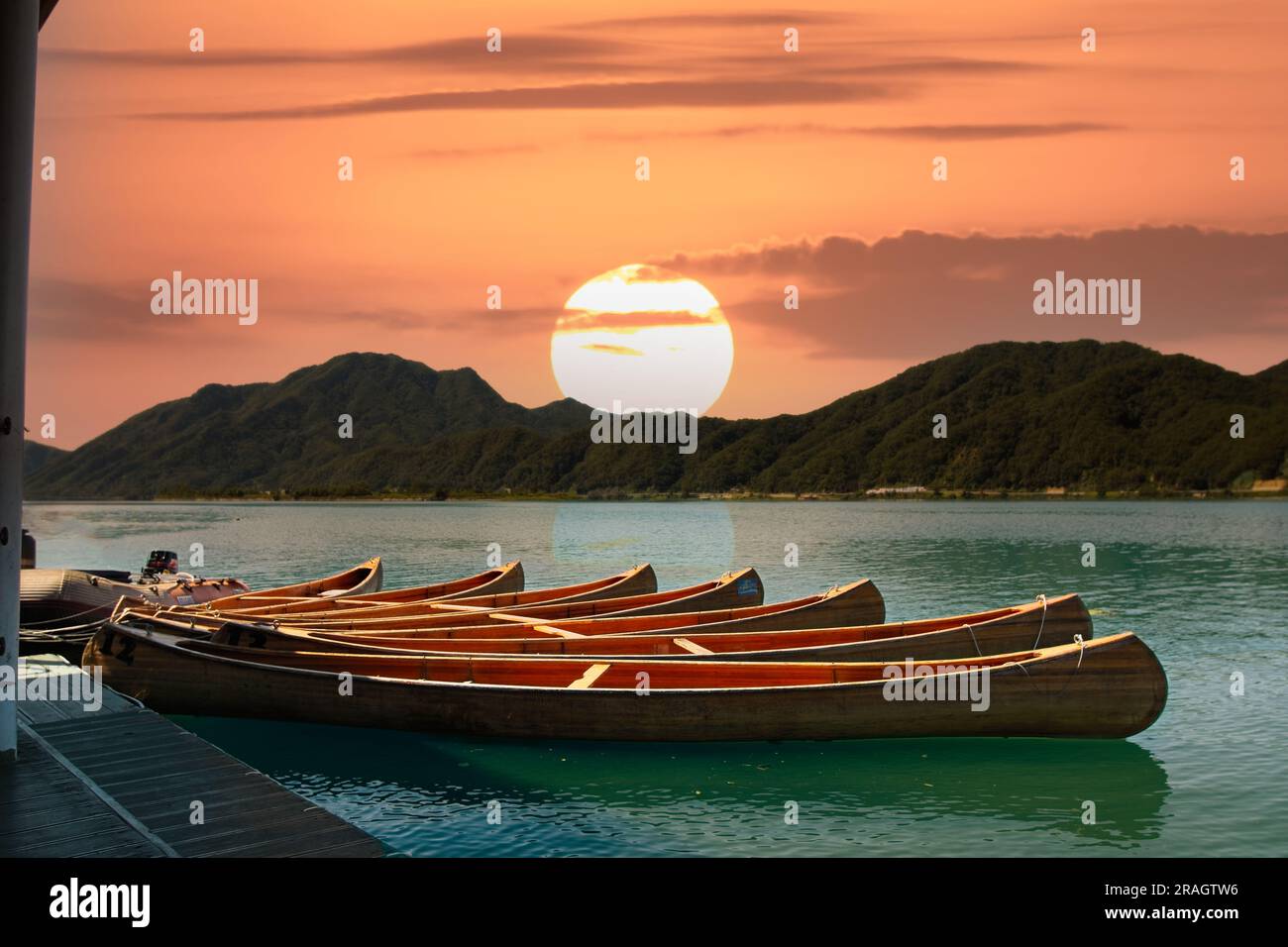 Orange canoes rest on the shore of a calm blue lake at sunset ...