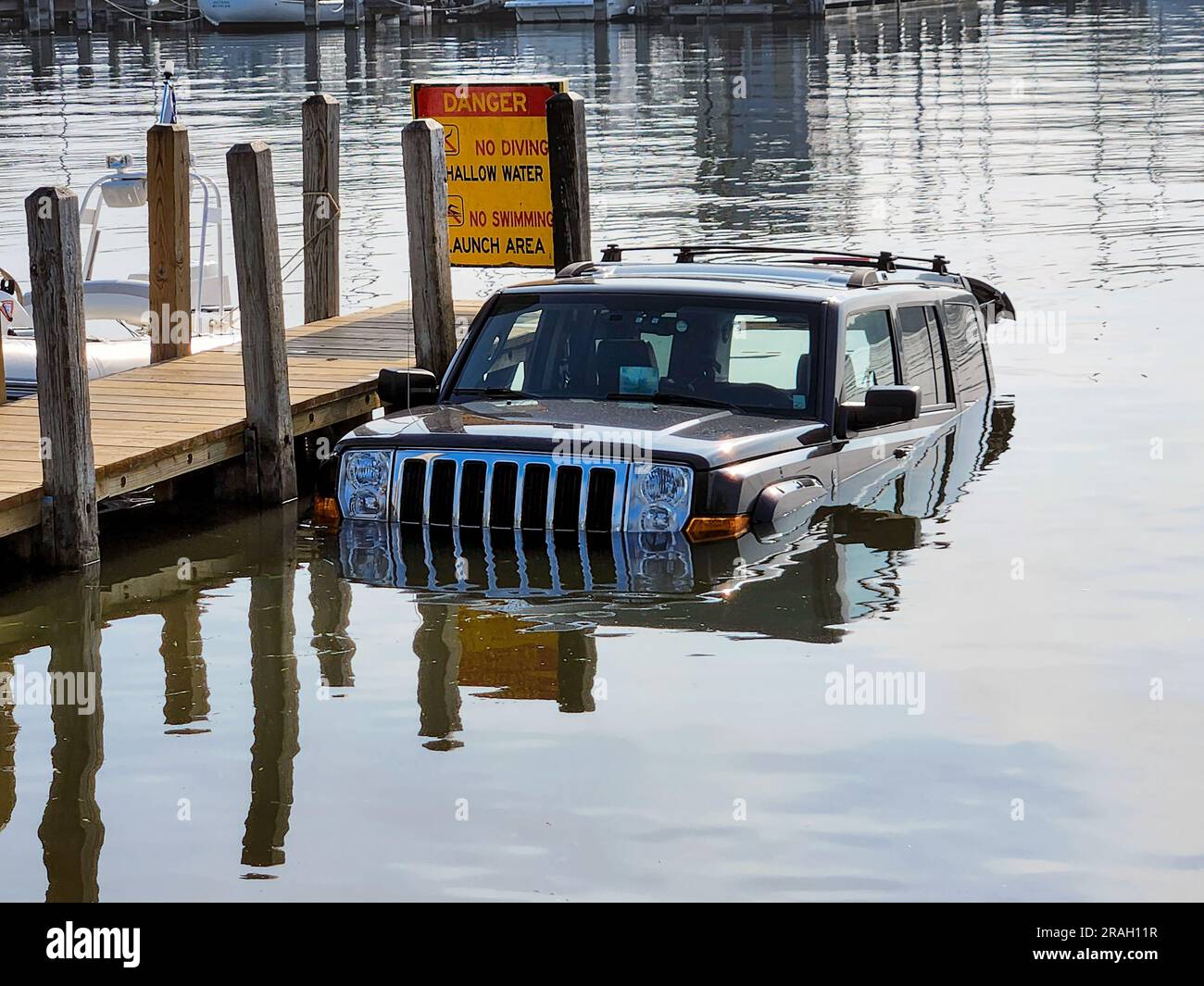 Black SUV vehicle half submerged in a lake water by a wooden dock Stock ...