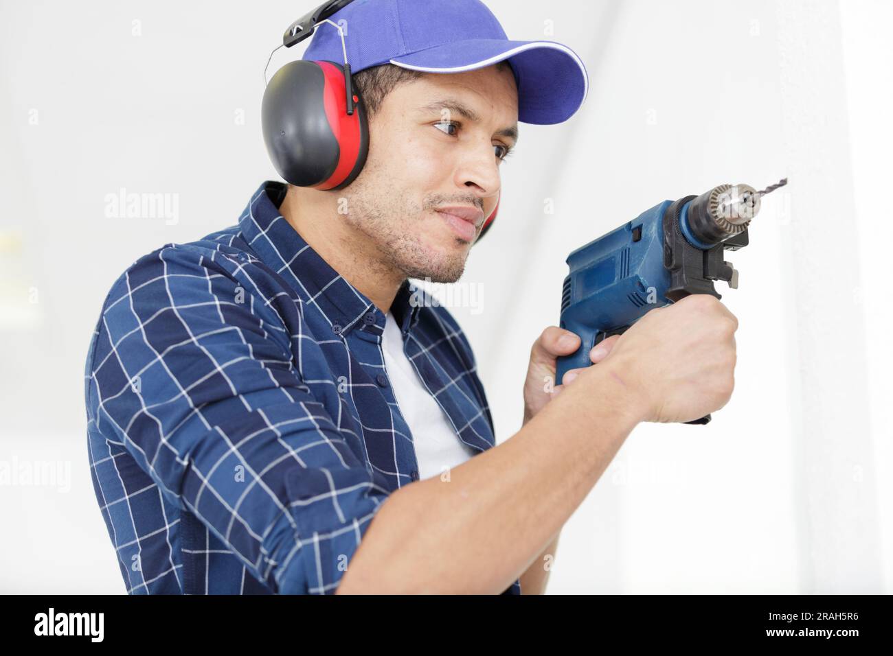 worker with electric drill perforator equipment making hole in wall ...