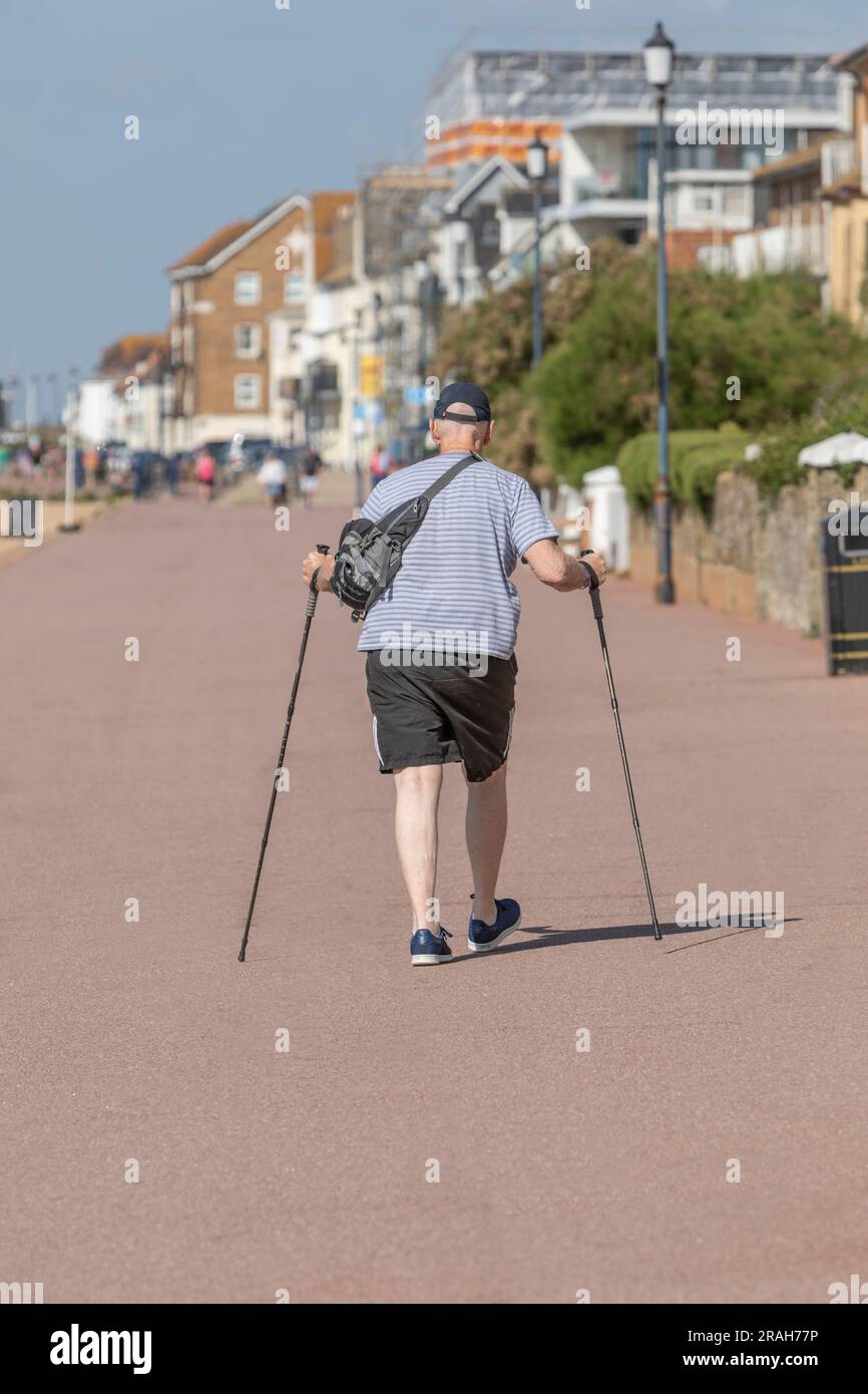 An old man walking along a seside promenade with two walking sticks ...