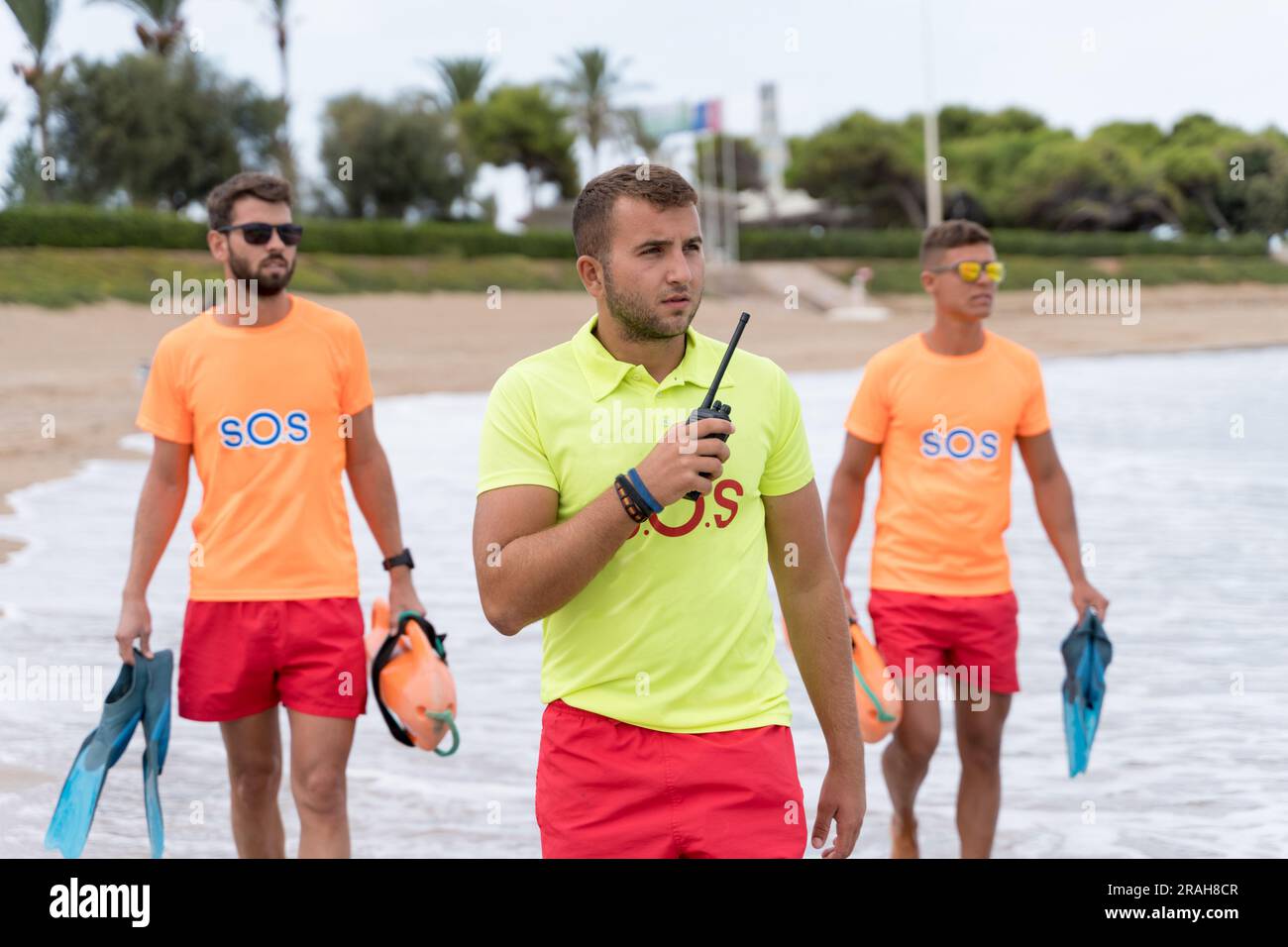 Portrait of three Lifeguards using a radio while walking along the ...