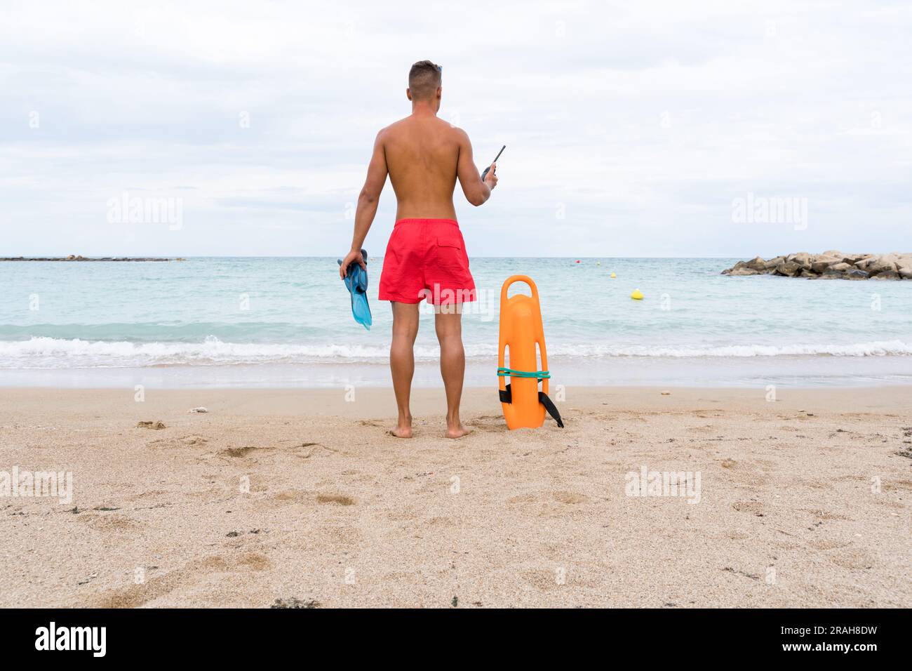 Rear view of a lifeguard standing on the beach using a radio Stock ...