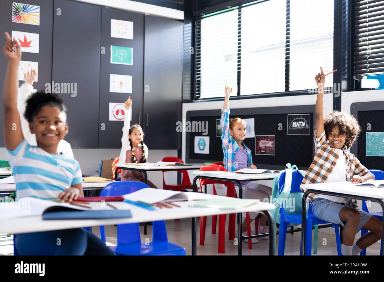 Diverse, happy schoolchildren raising hands in elementary school ...