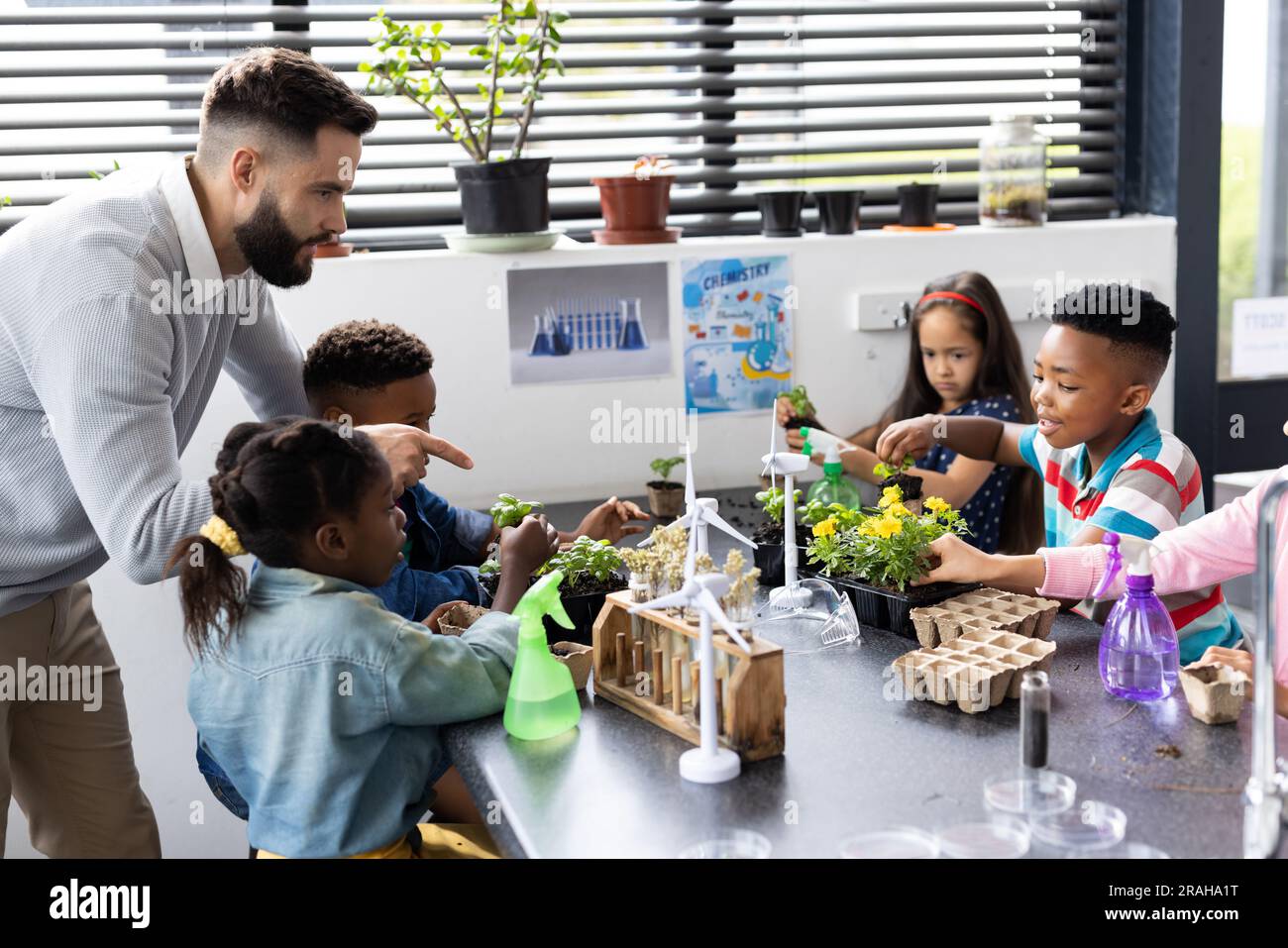 Diverse elementary schoolchildren and male teacher studying plants ...
