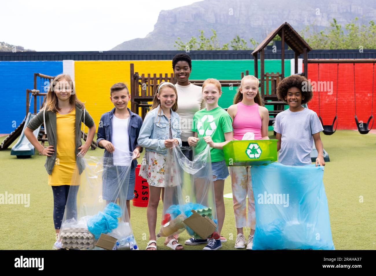 Portrait of happy diverse female teacher and pupils holding recycling ...