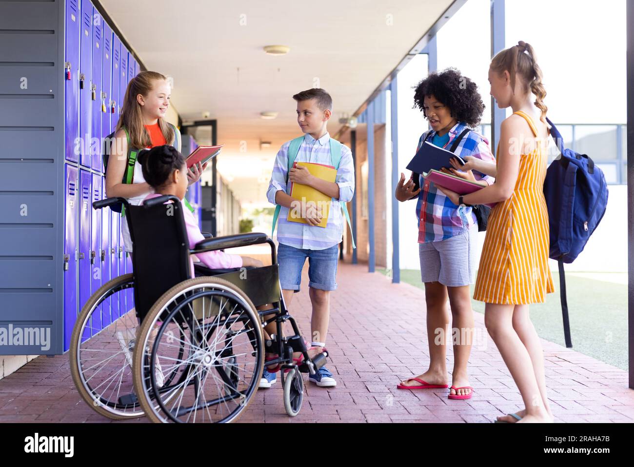 Happy diverse school children talking with girl in wheelchair in school ...
