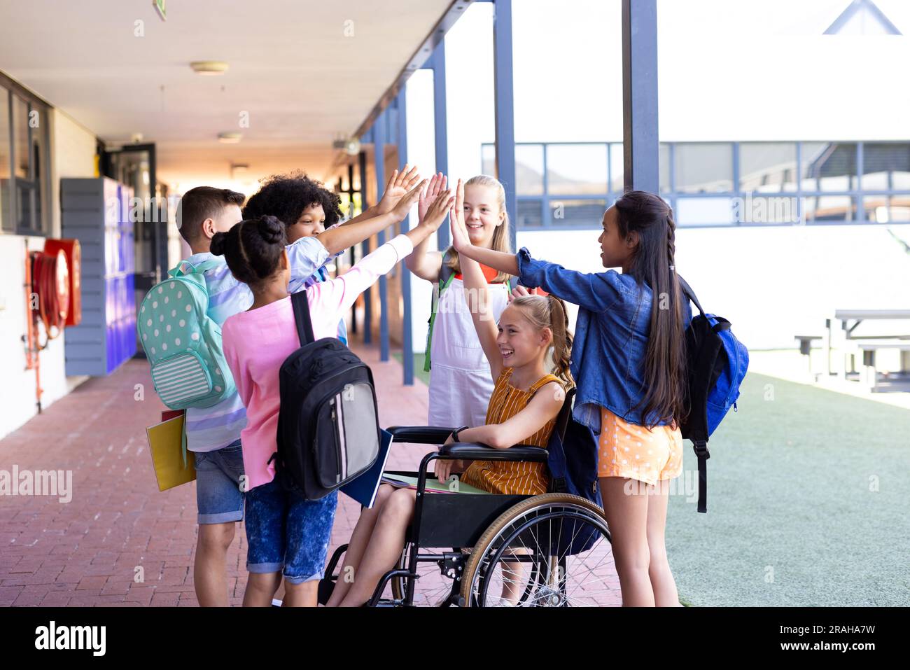 Happy diverse school children high fiving with girl in wheelchair in ...