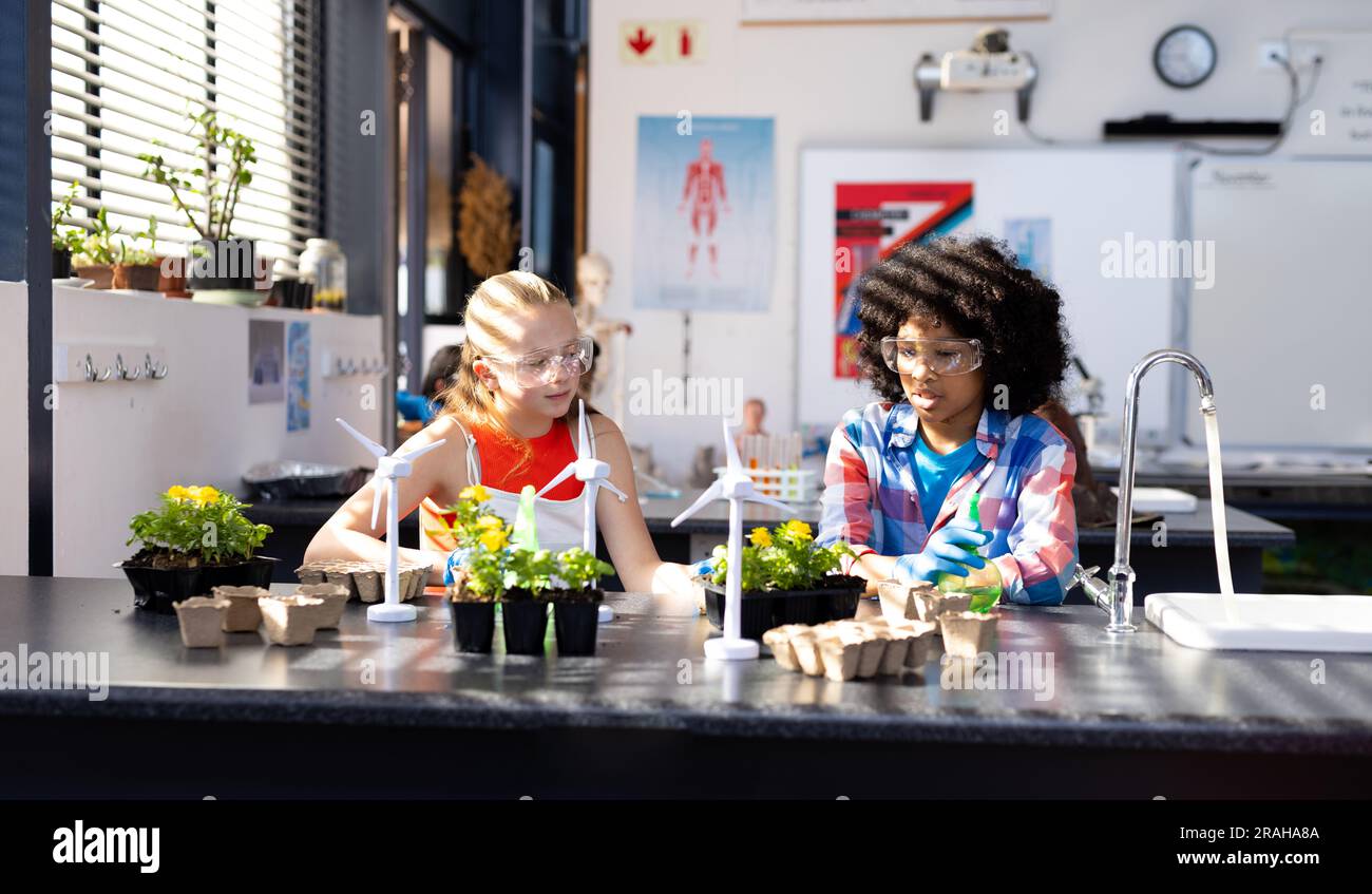 Two happy diverse schoolgirls studying plants and wind turbines in ...