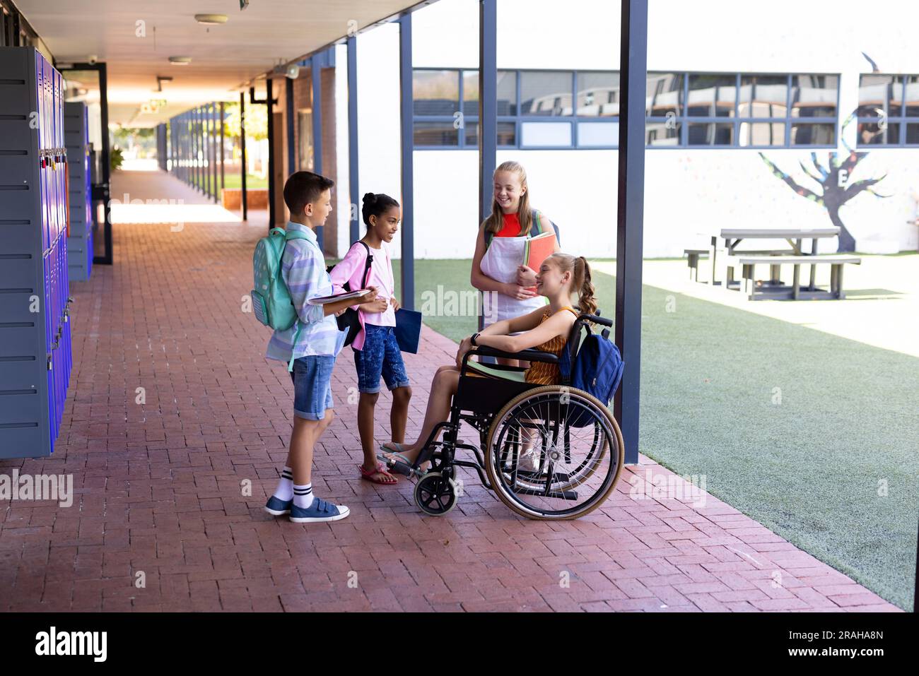 Happy diverse school children talking with girl in wheelchair in school ...