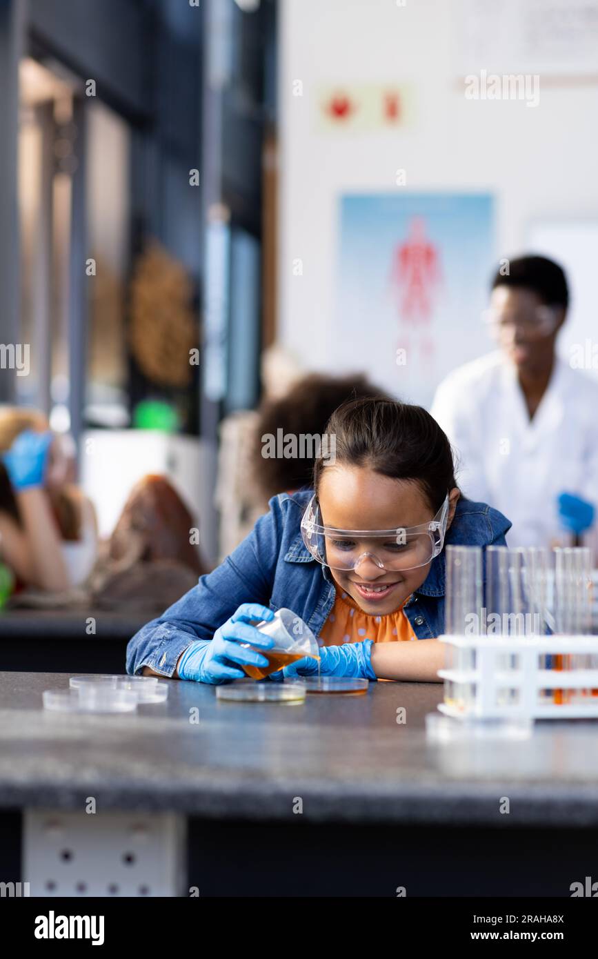 Vertical of happy biracial schoolgirl doing an experiment in chemistry ...