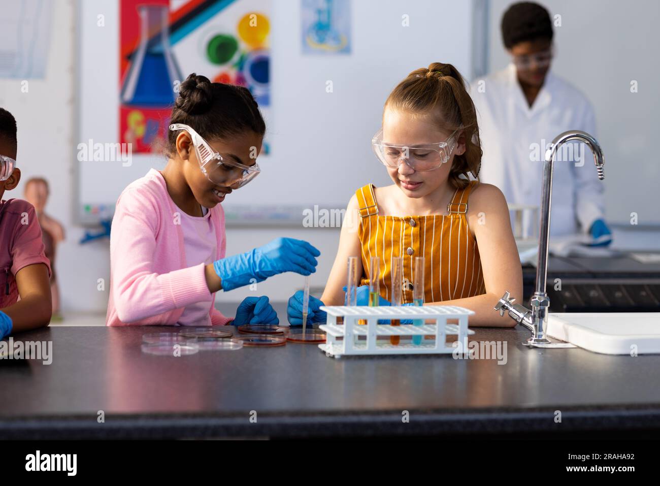 Two happy diverse schoolgirls doing an experiment in chemistry class ...