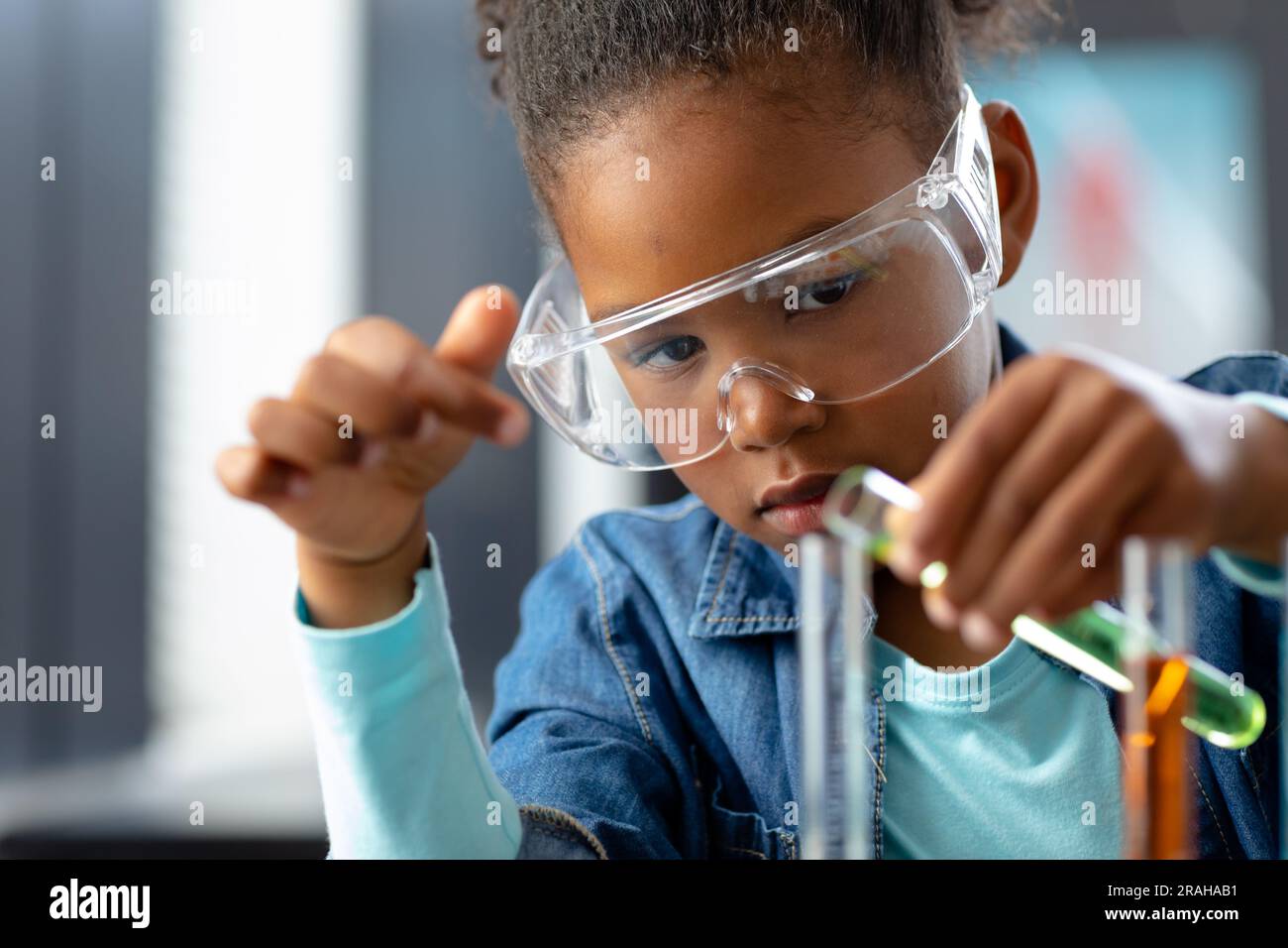 Serious biracial schoolgirl in safety glasses doing experiment in ...