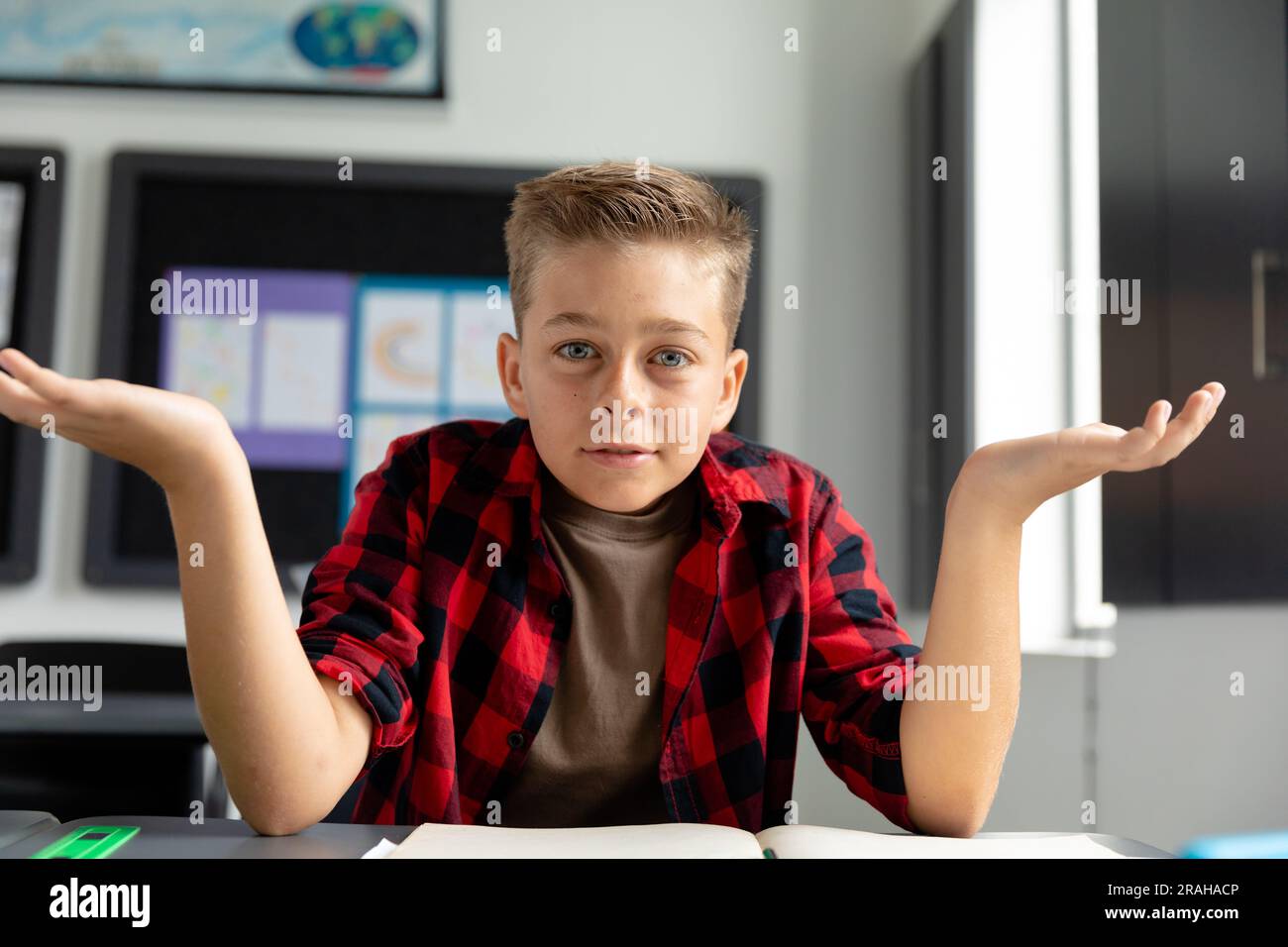 Portrait of confused caucasian schoolboy at desk, shrugging shoulders ...