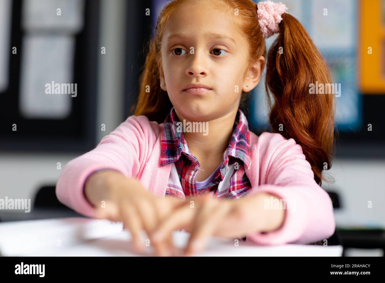 Blind, biracial schoolgirl sitting at desk reading braille in class ...