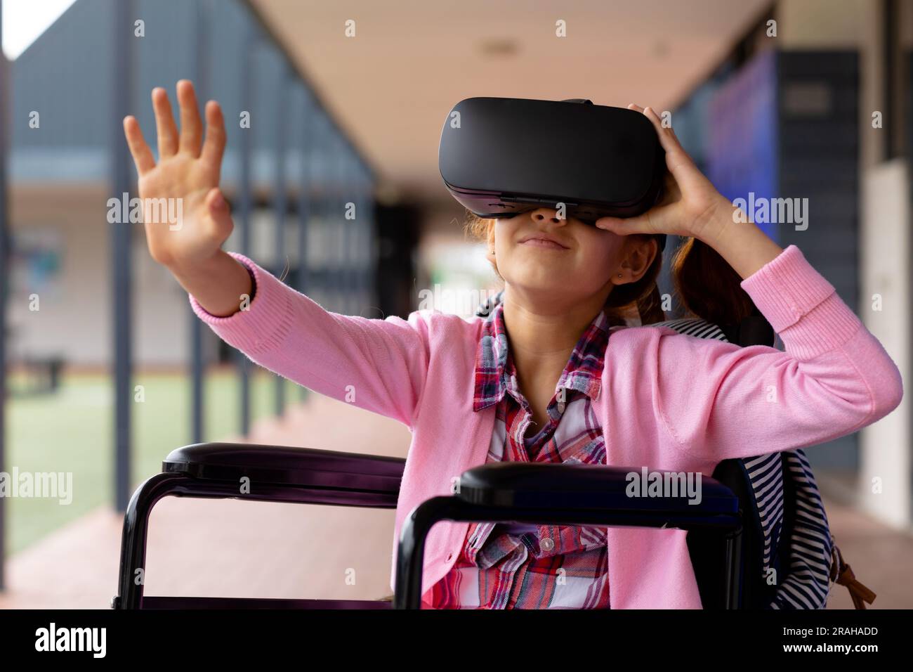 Biracial girl in wheelchair, using vr headset, with hand out, in school ...