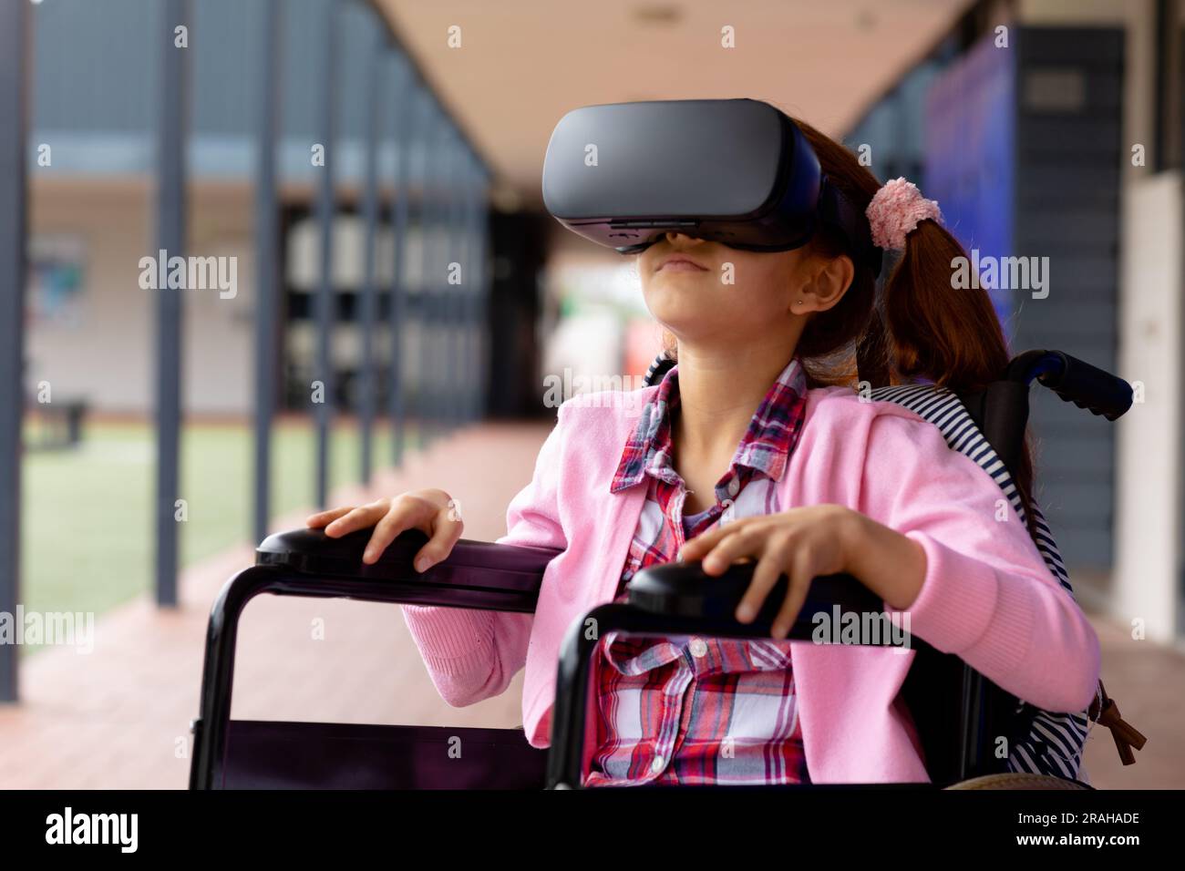 Happy biracial schoolgirl in wheelchair, using vr headset in school ...