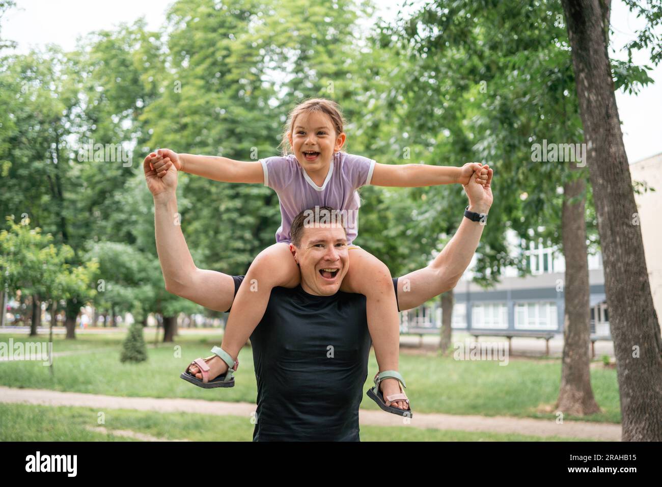 Child girl piggybacks on father, riding on father's shoulder in park ...