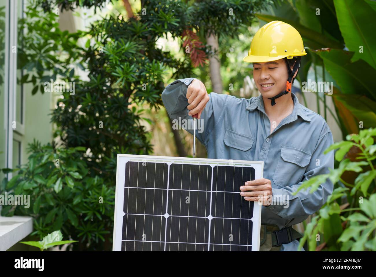 Portrait of smiling solar panel installer wearing hardhat screwing ...