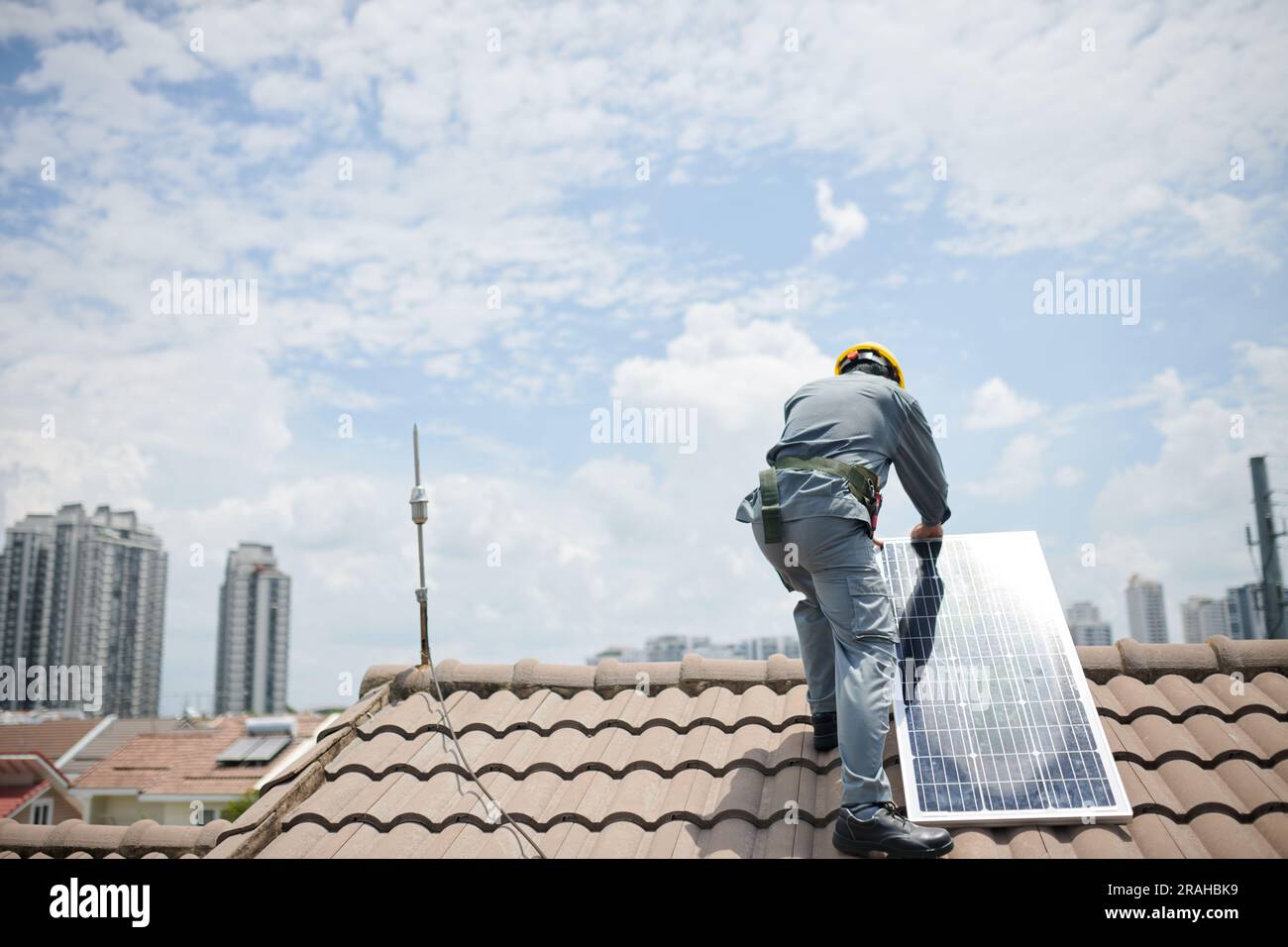 Worker in hardhat and grey uniform installing solar panel on roof Stock ...