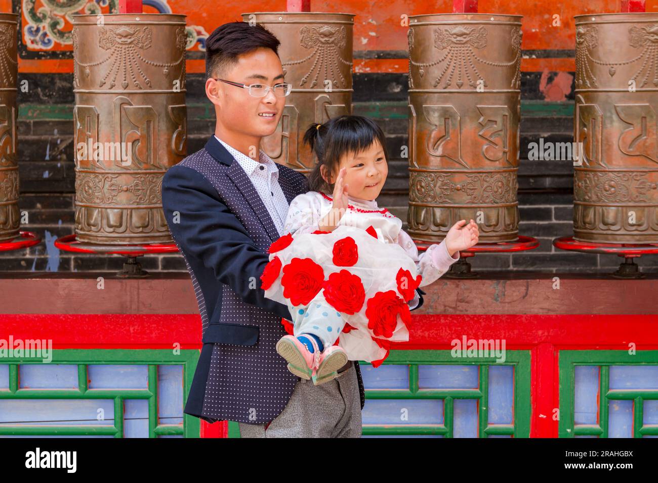 A dad and a young girl pose in front of aniken prayer wheels of a ...