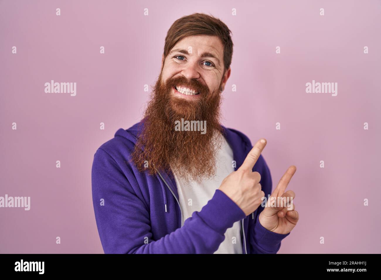Caucasian man with long beard standing over pink background smiling and ...