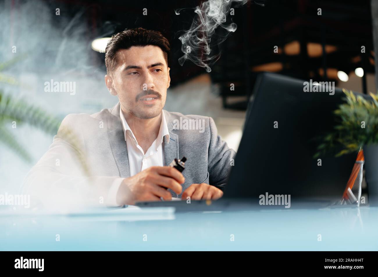 Young businessman smoking an electronic cigarette in his office while ...