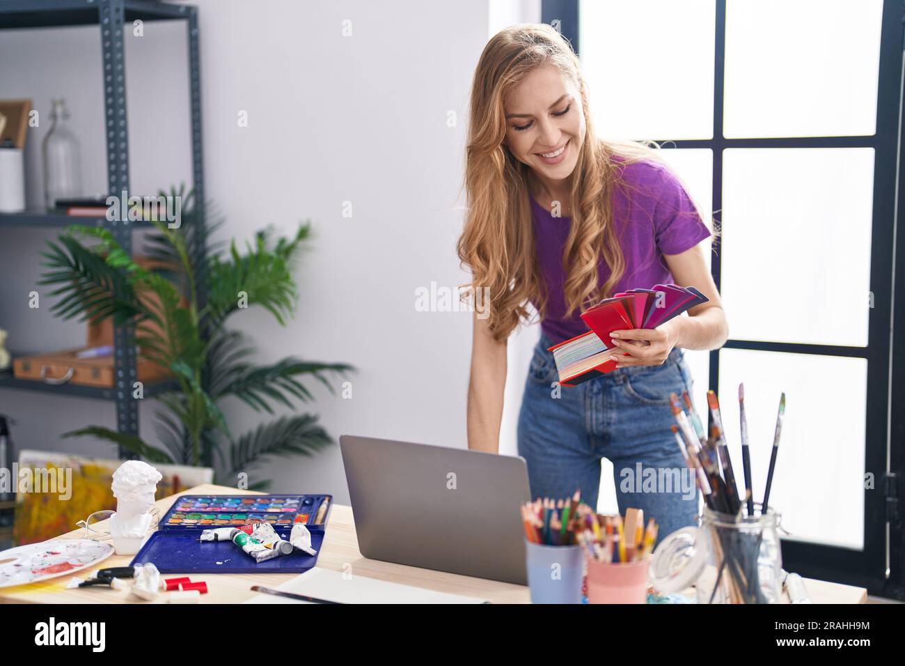 Young blonde woman artist choosing color using laptop at art studio ...