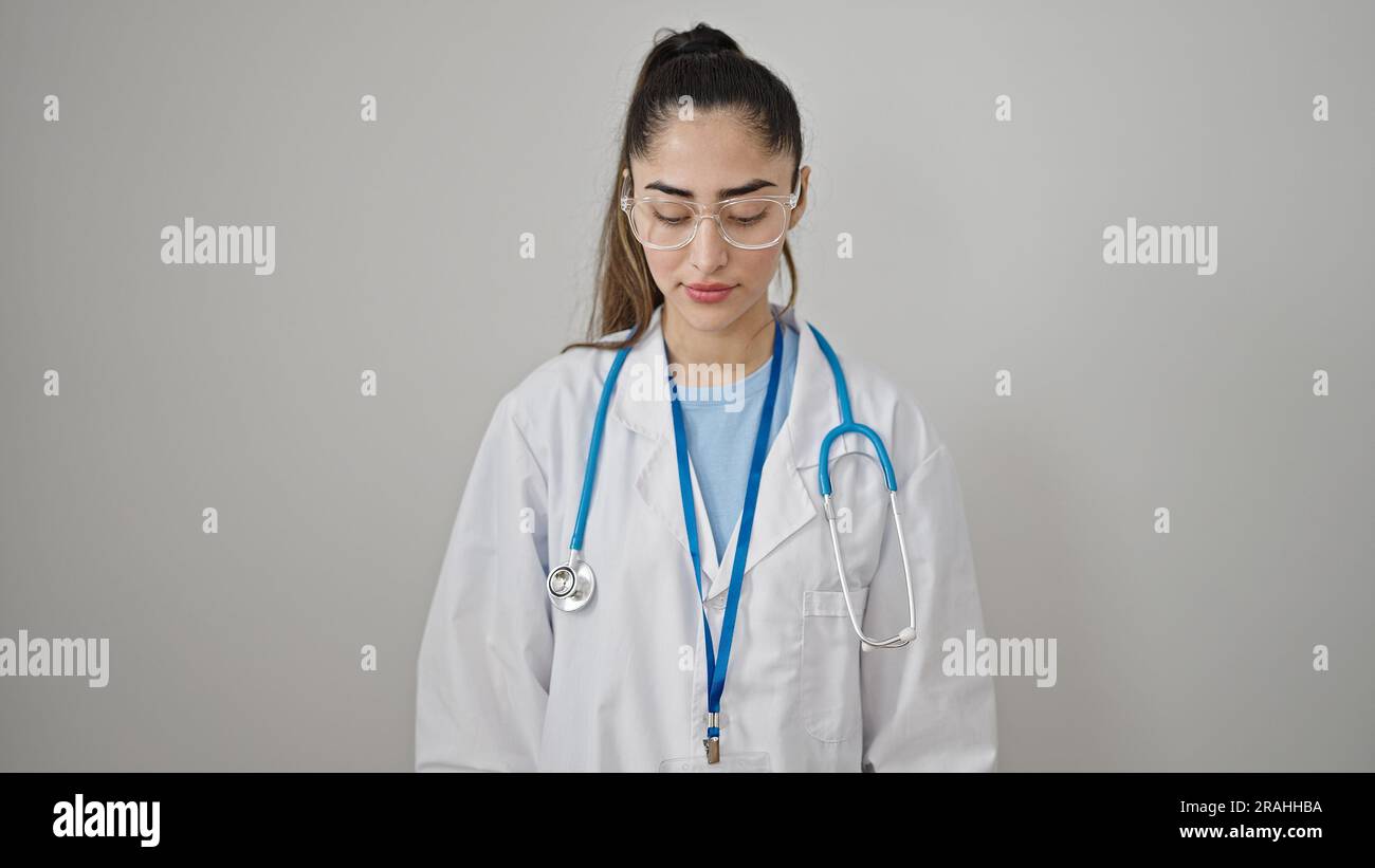 Young beautiful hispanic woman doctor looking down with serious ...