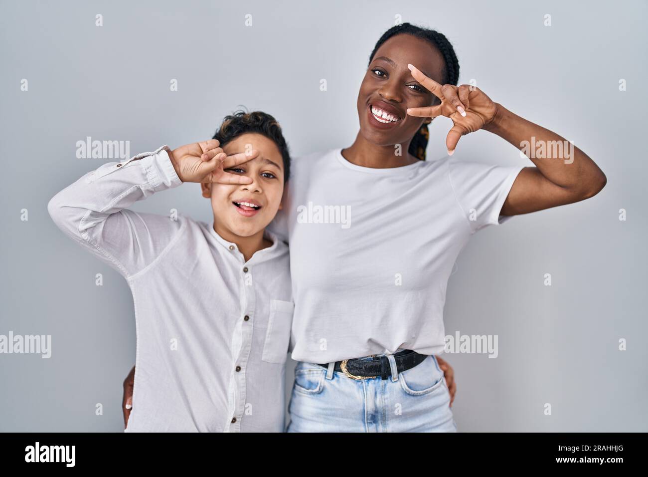 Young mother and son standing together over white background doing ...