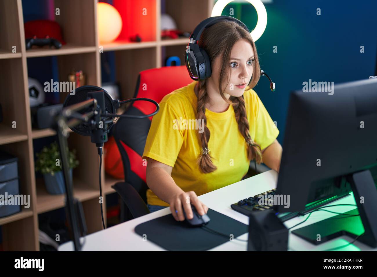 Young blonde woman streamer playing video game using computer at gaming ...