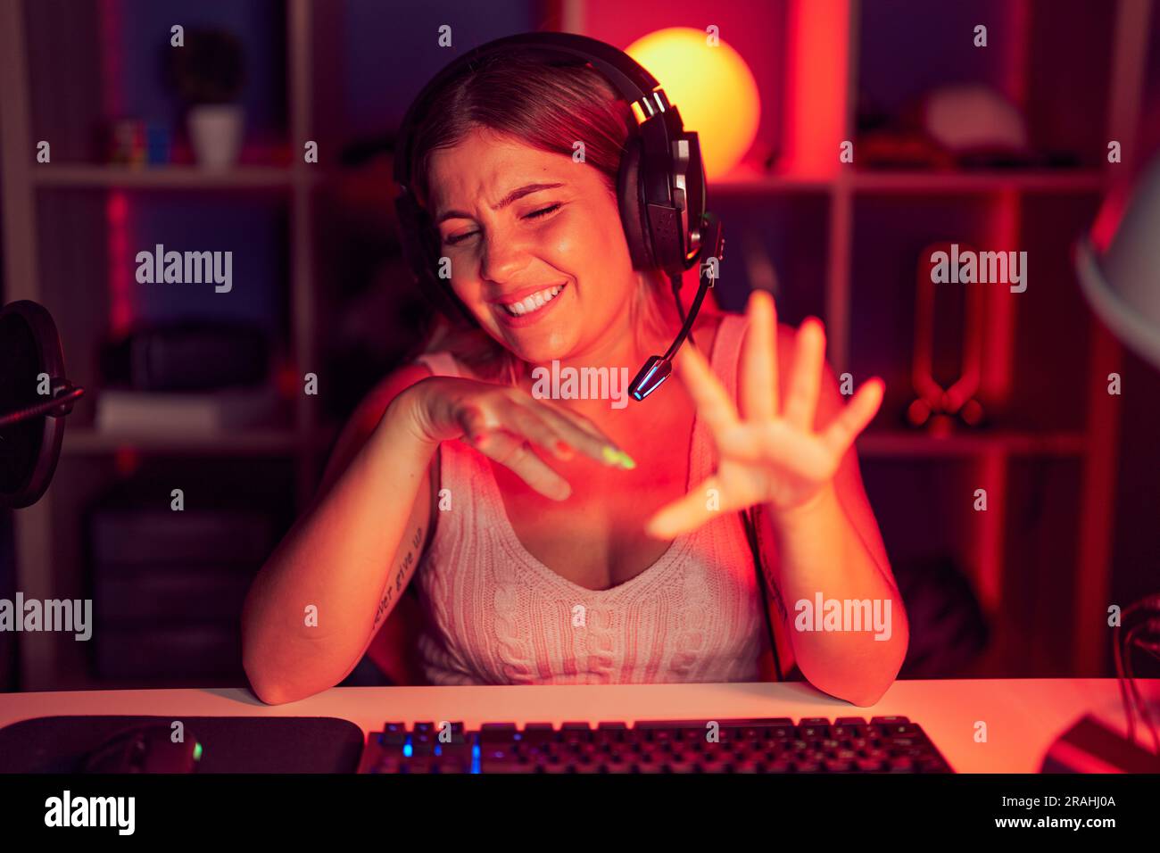 Young blonde woman playing video games wearing headphones disgusted ...