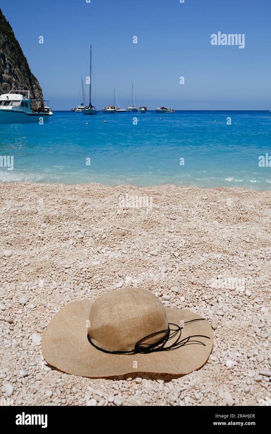 straw hat on Navagio beach with high cliff and turquoise water ...