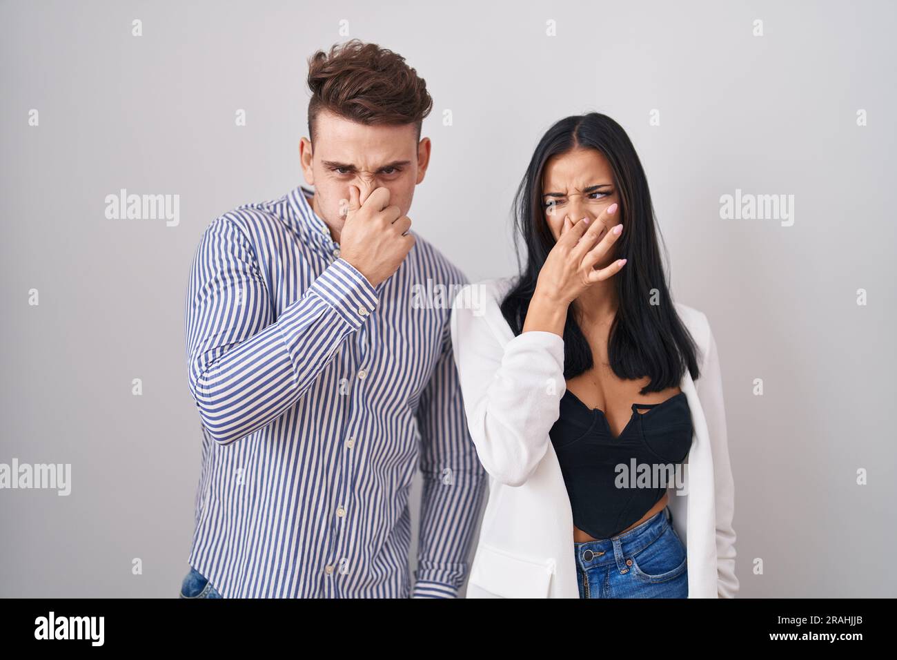Young hispanic couple standing over white background smelling something ...