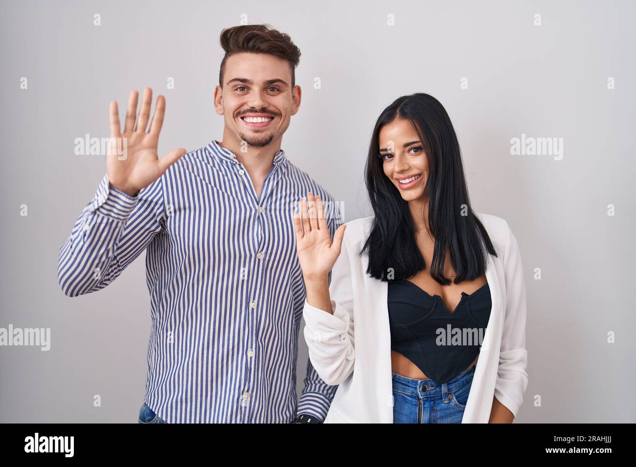 Young hispanic couple standing over white background waiving saying ...