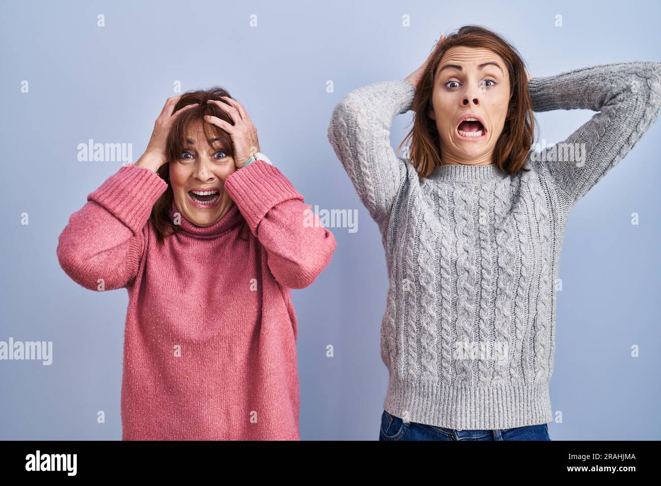Mother and daughter standing over blue background crazy and scared with ...