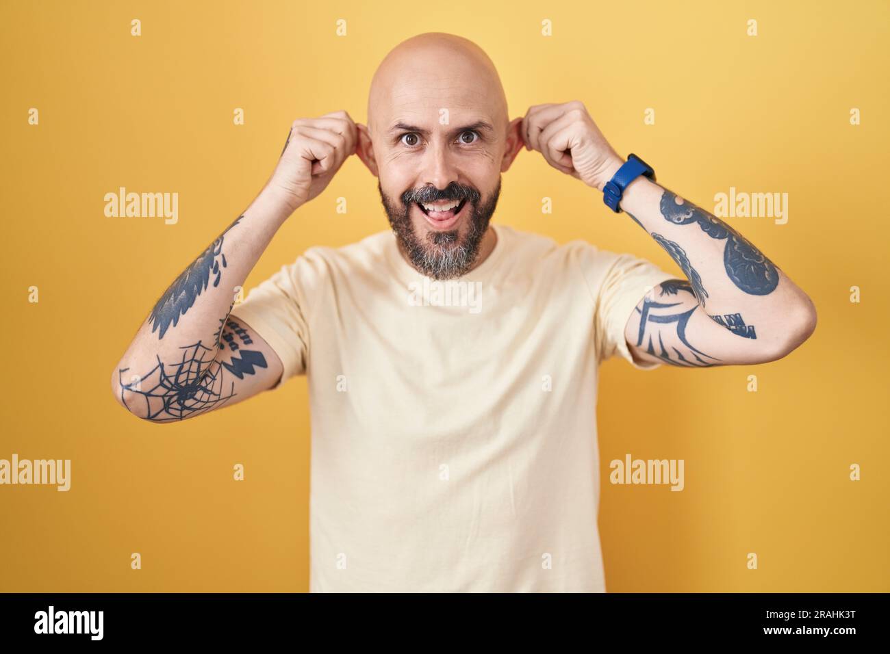 Hispanic man with tattoos standing over yellow background smiling ...