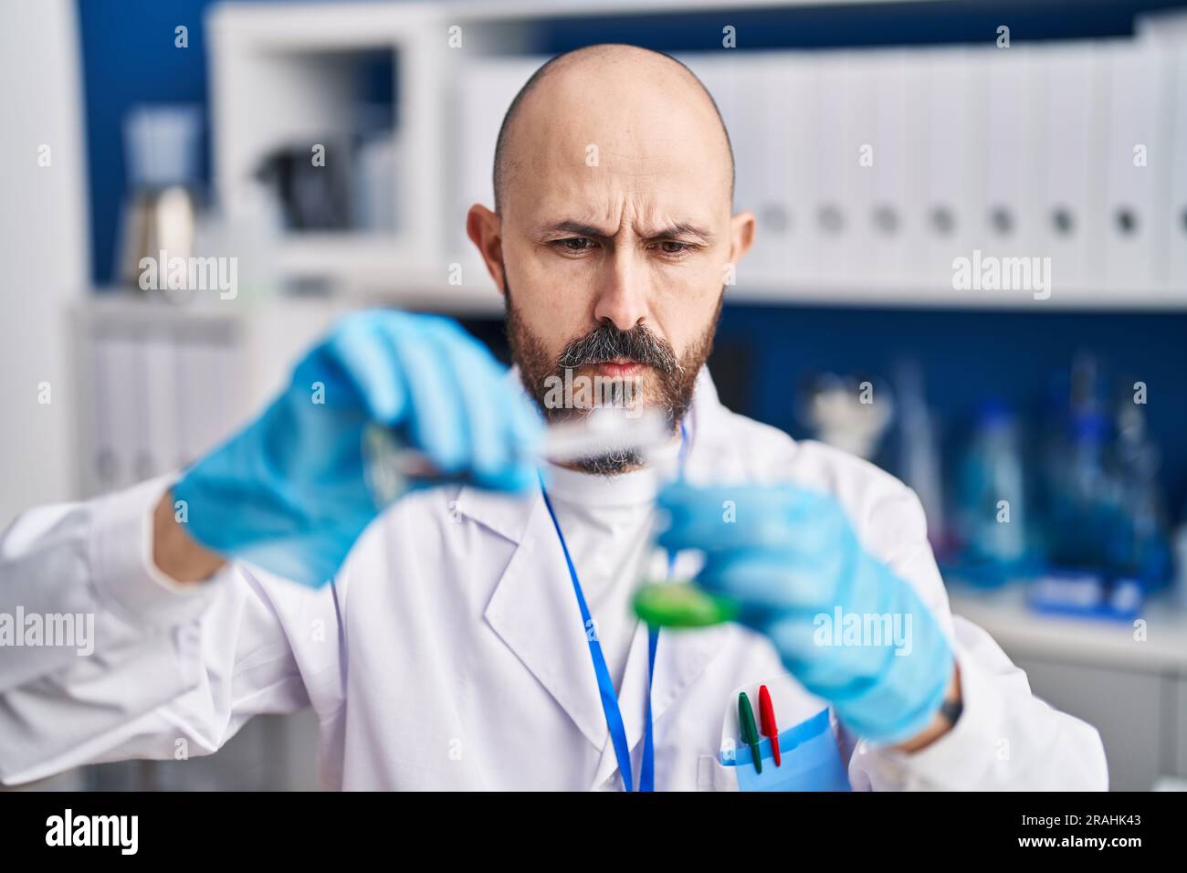 Young bald man scientist pouring liquid on test tube at laboratory ...