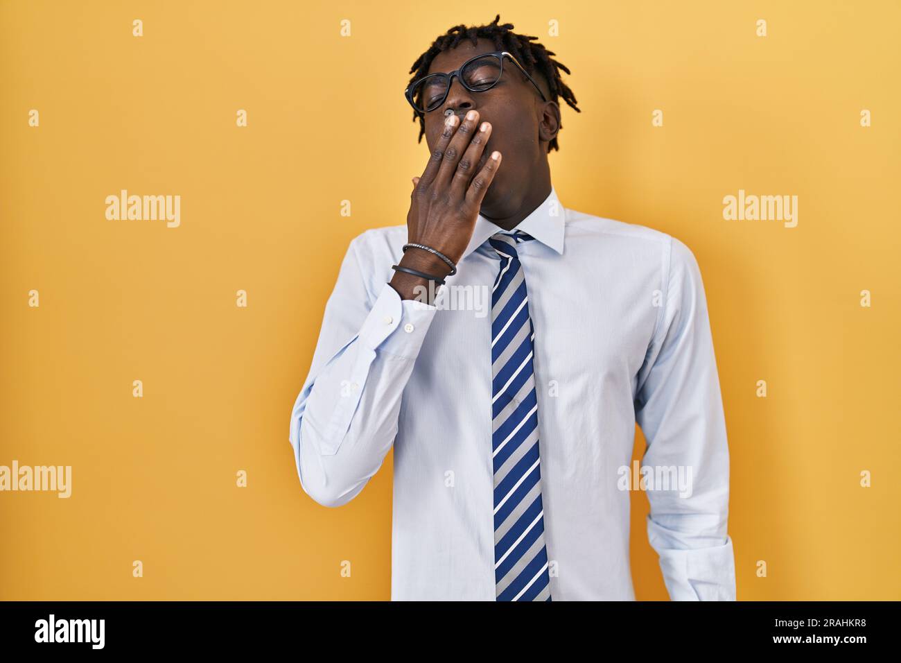 African man with dreadlocks standing over yellow background bored ...