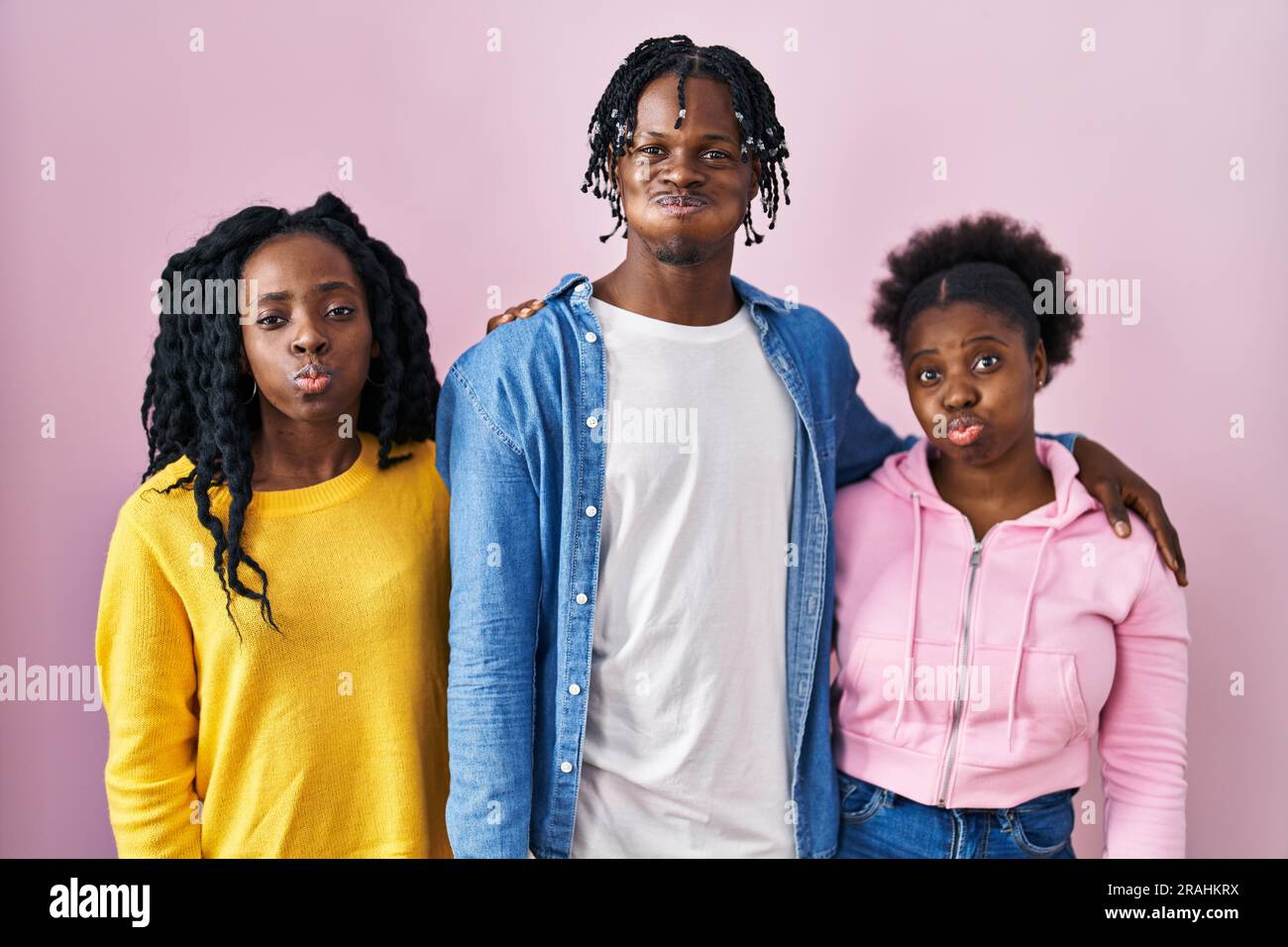Group of three young black people standing together over pink ...