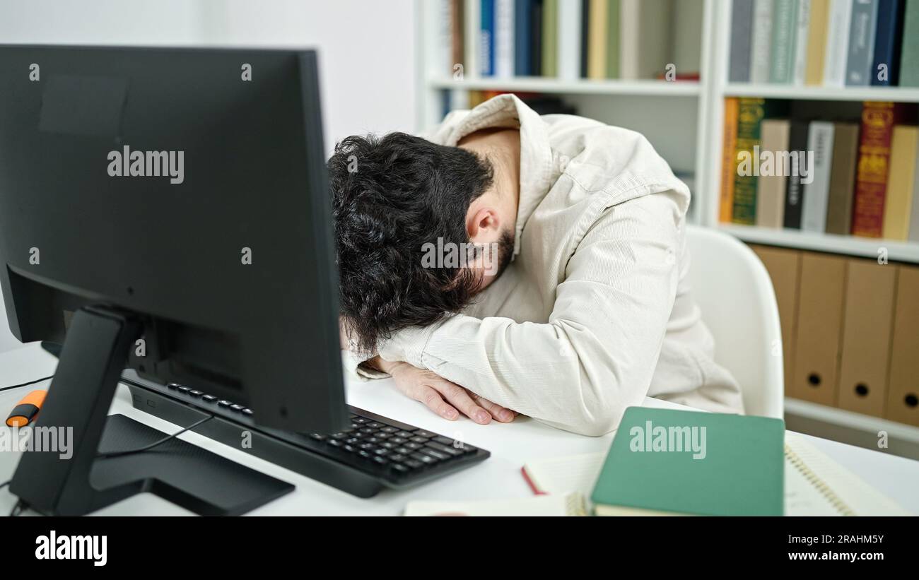 Young hispanic man student stressed using computer studying at library ...