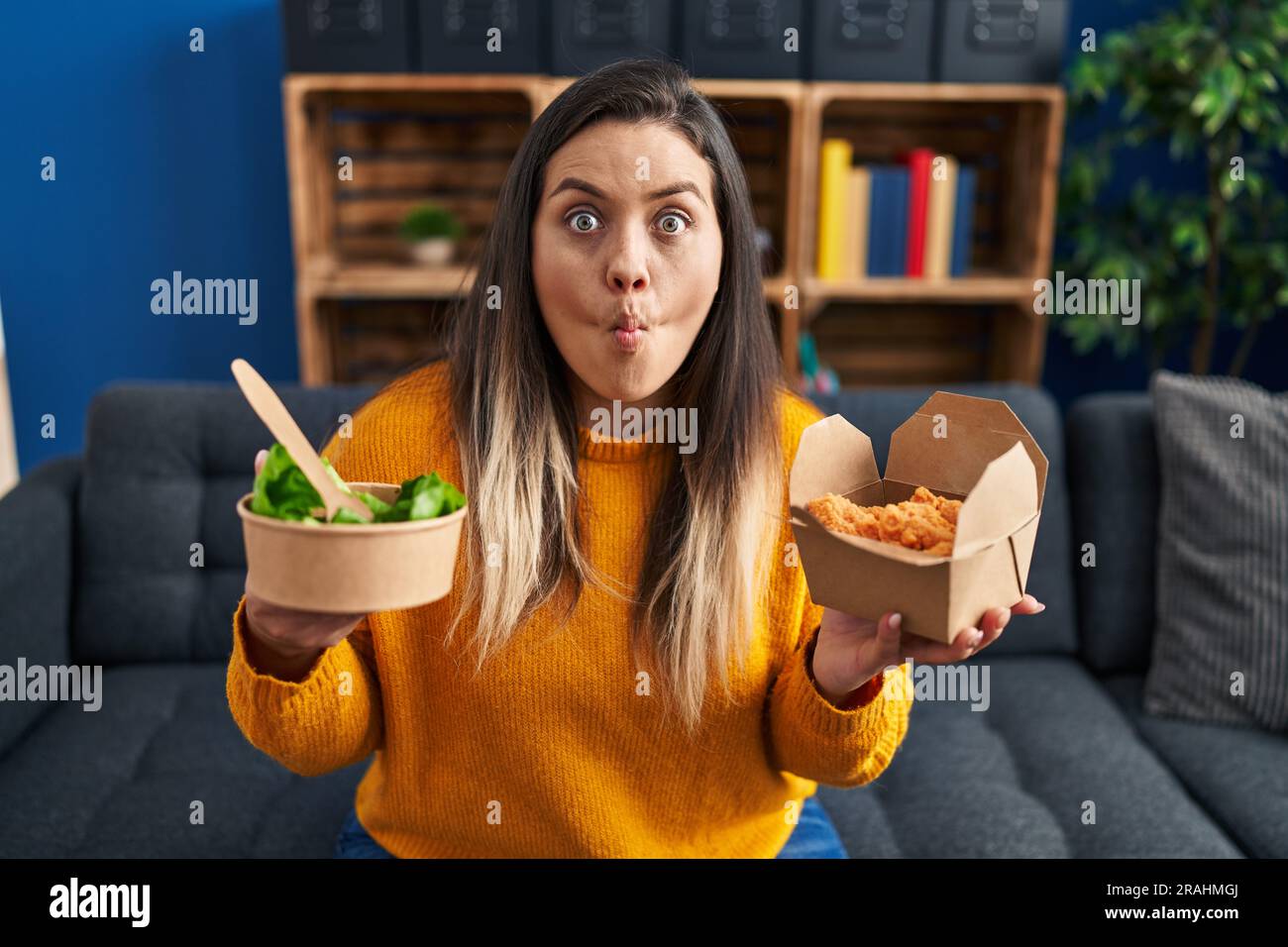Young hispanic woman holding healthy salad and fried chicken wings ...