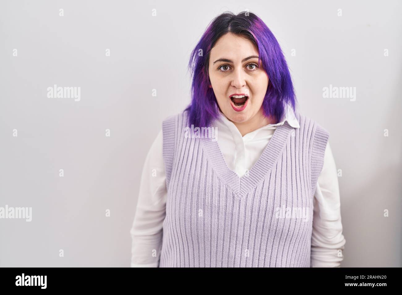 Plus size woman wit purple hair standing over white background afraid ...